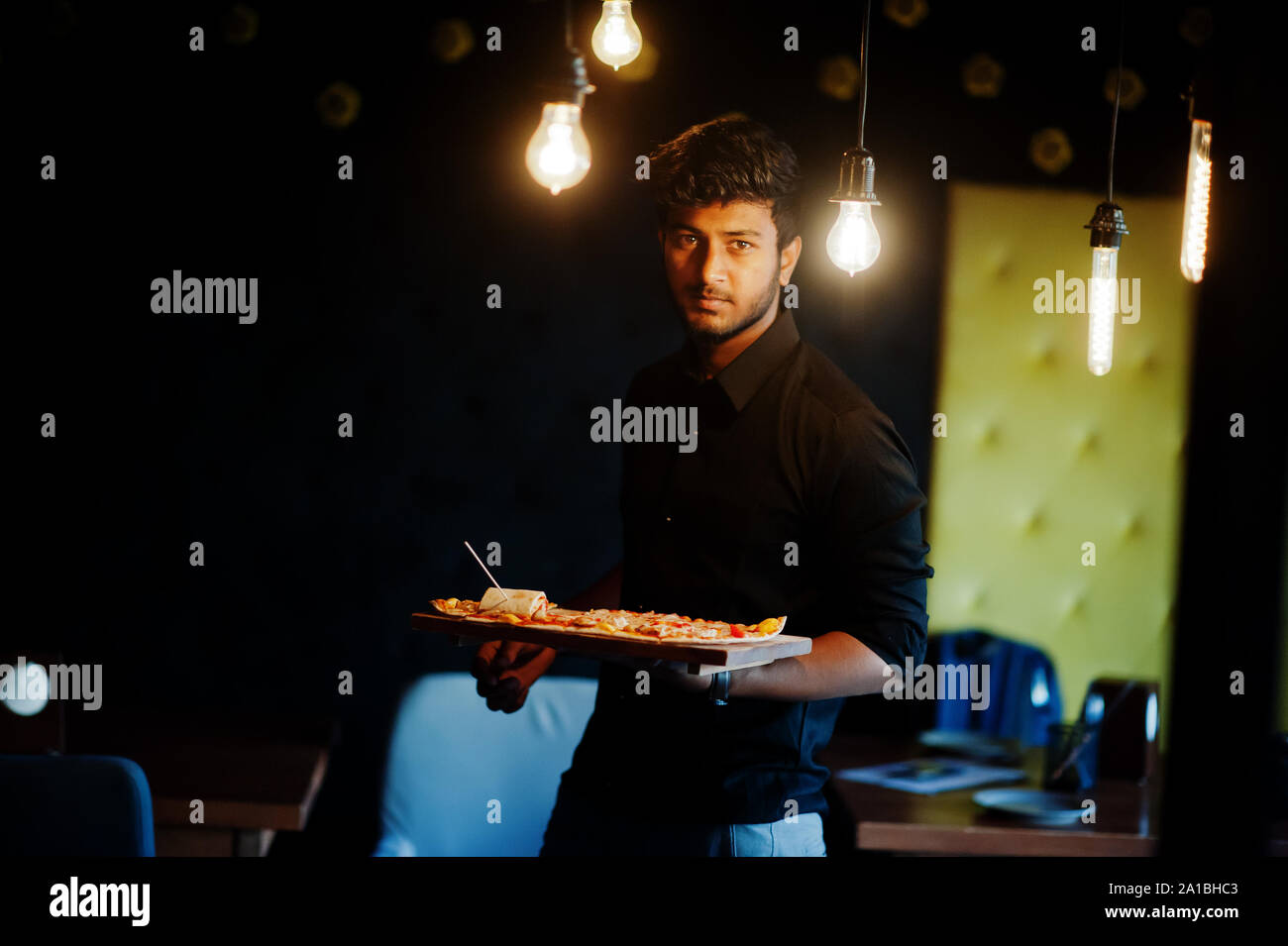 Confident young indian man in black shirt standing at pizzeria with ...