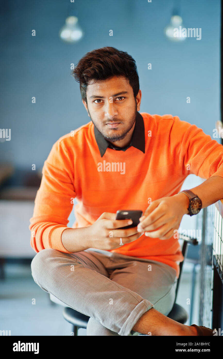 Confident young indian man in orange sweater sitting bar counter at ...