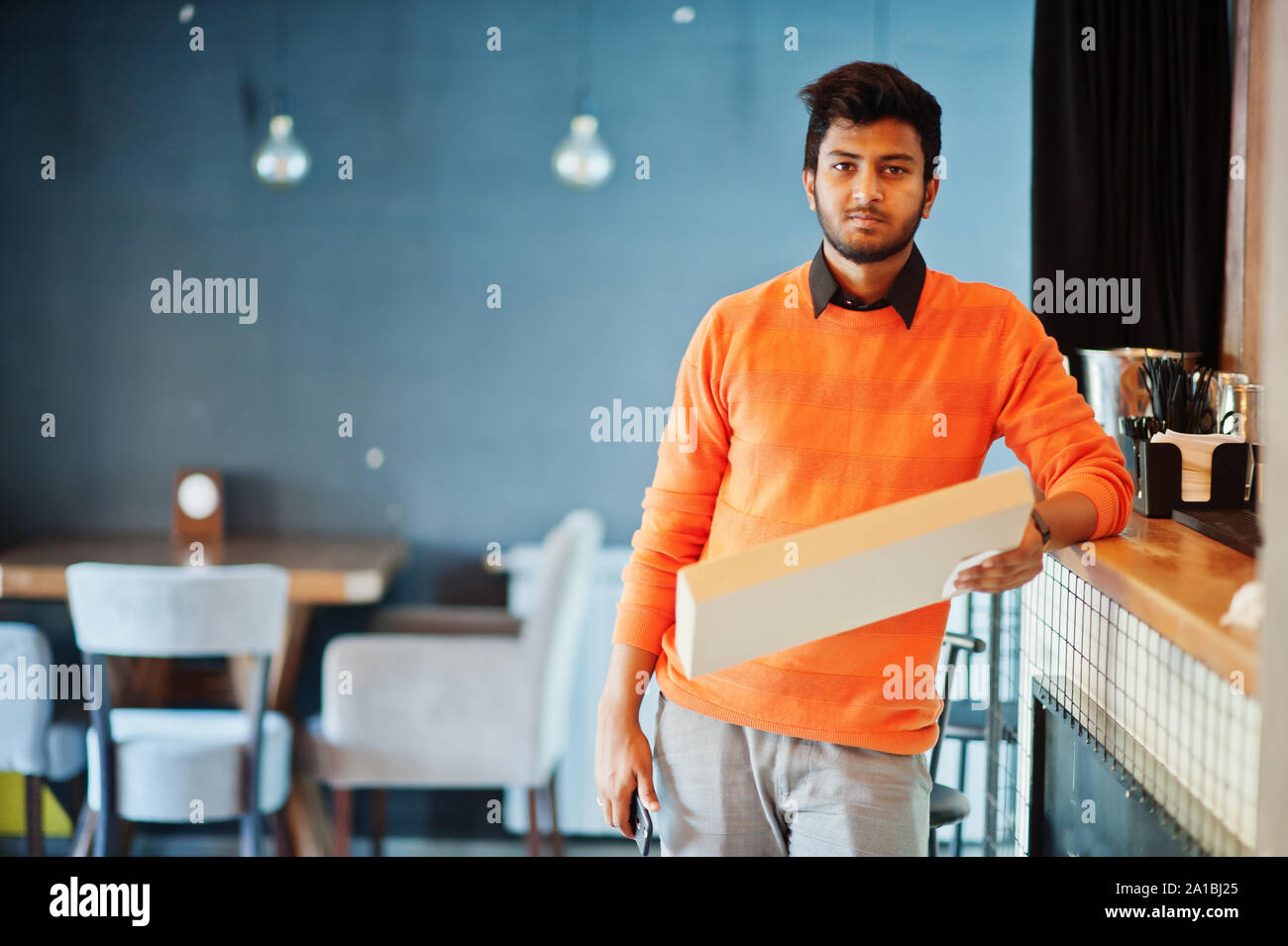Confident young indian man in orange sweater standing near bar counter ...