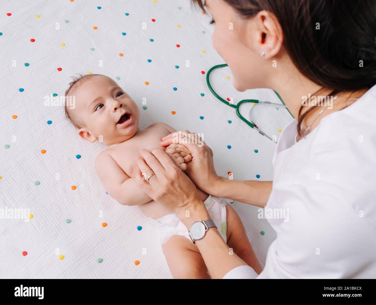 Doctor entertains baby to exam her with stethoscope on a special table ...