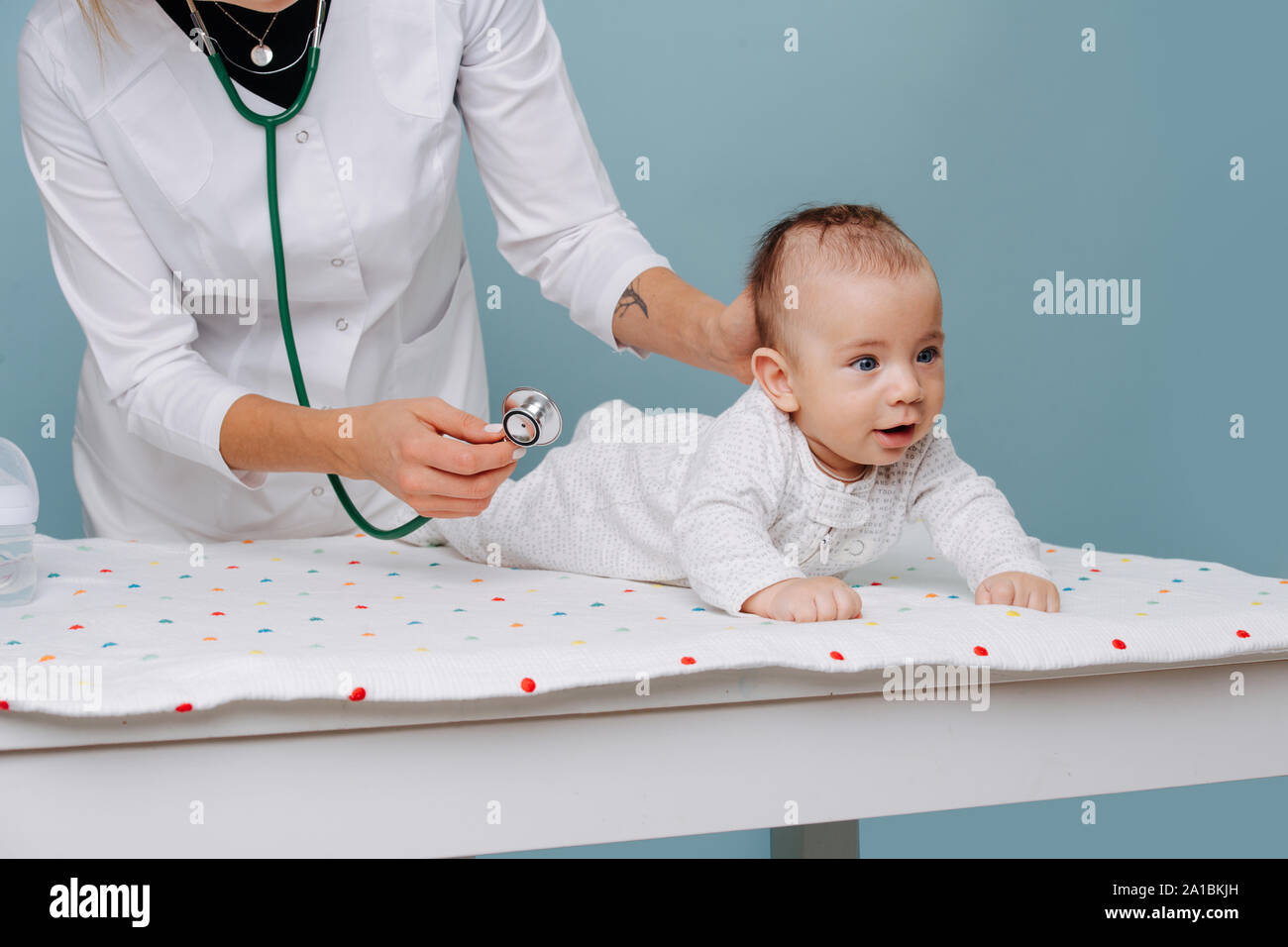 Doctor exams baby with stethoscope on a special table over blue ...
