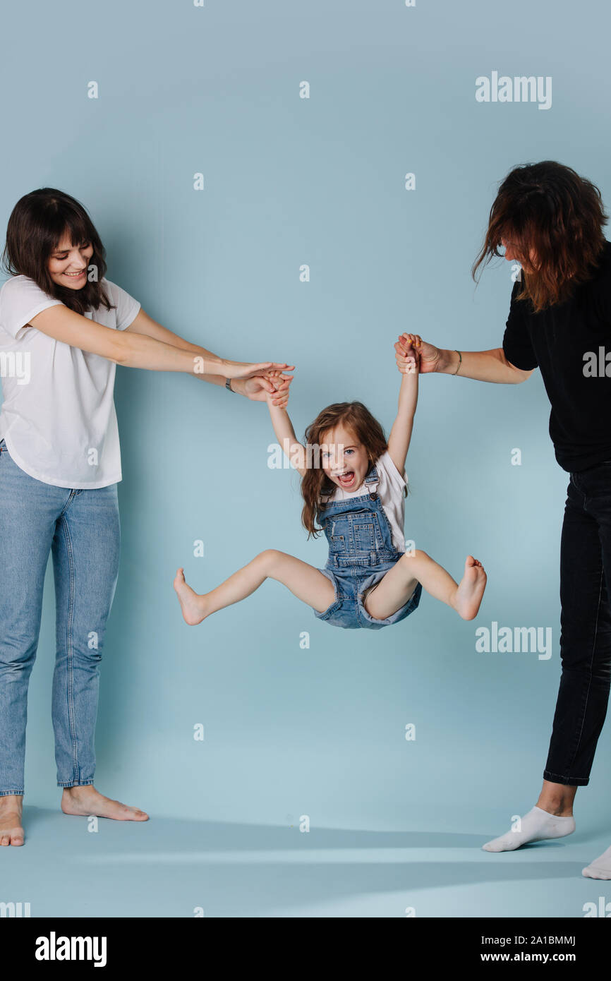 Two adults lifting little girl by hands for her amusement over blue ...