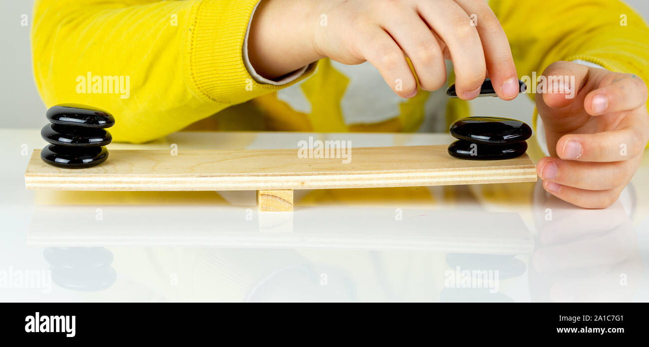 child posing balancing black pebbles on a wooden scale Stock Photo - Alamy
