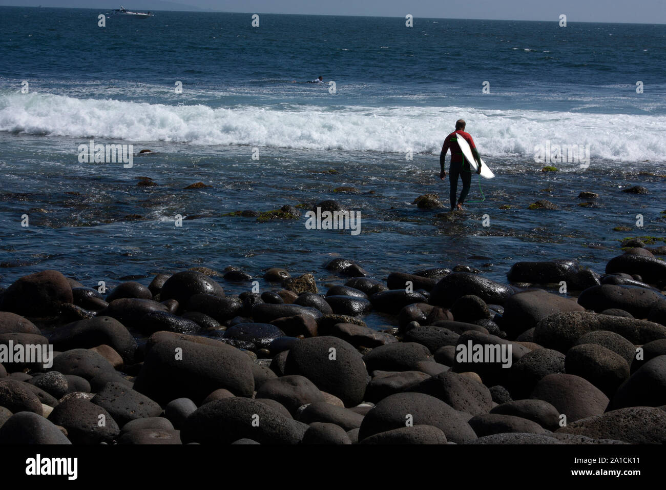 Man walking between rocks and water loading his surfboard to go surfing ...