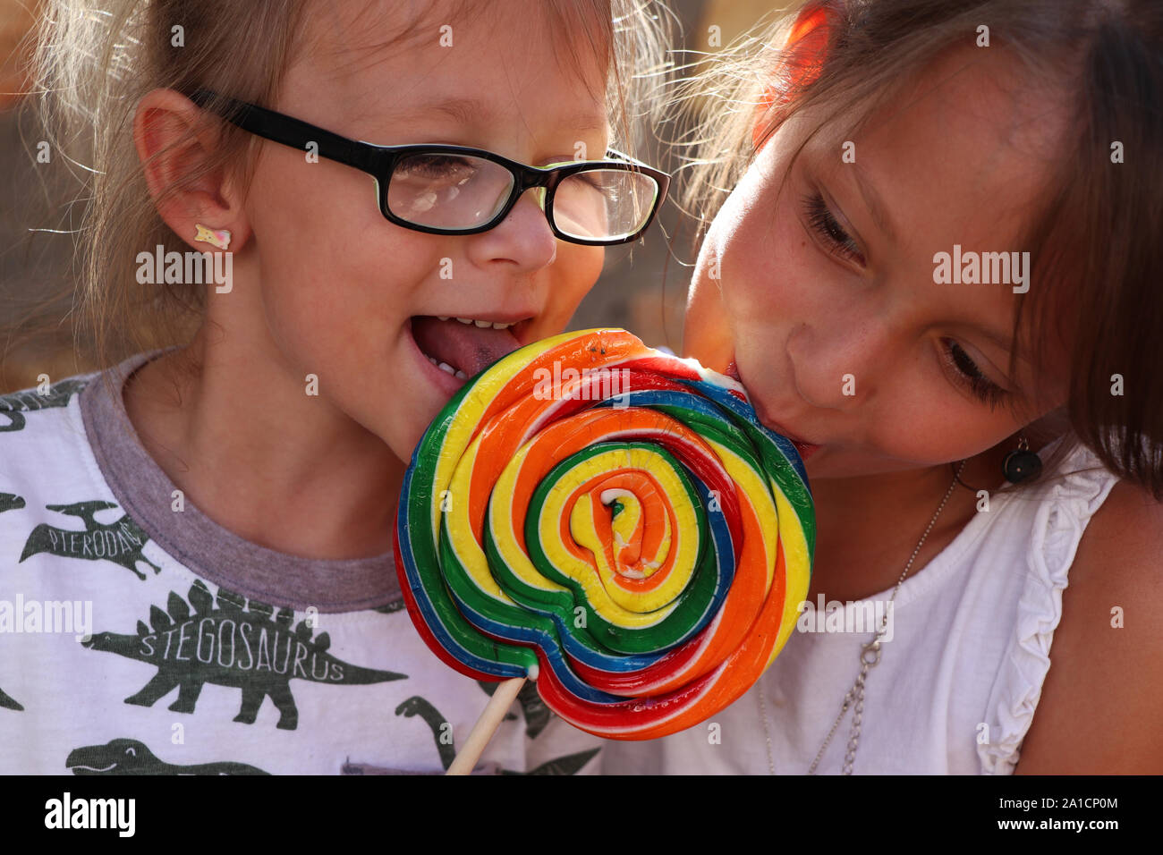 Two sisters sharing a colorful lollipop Stock Photo - Alamy