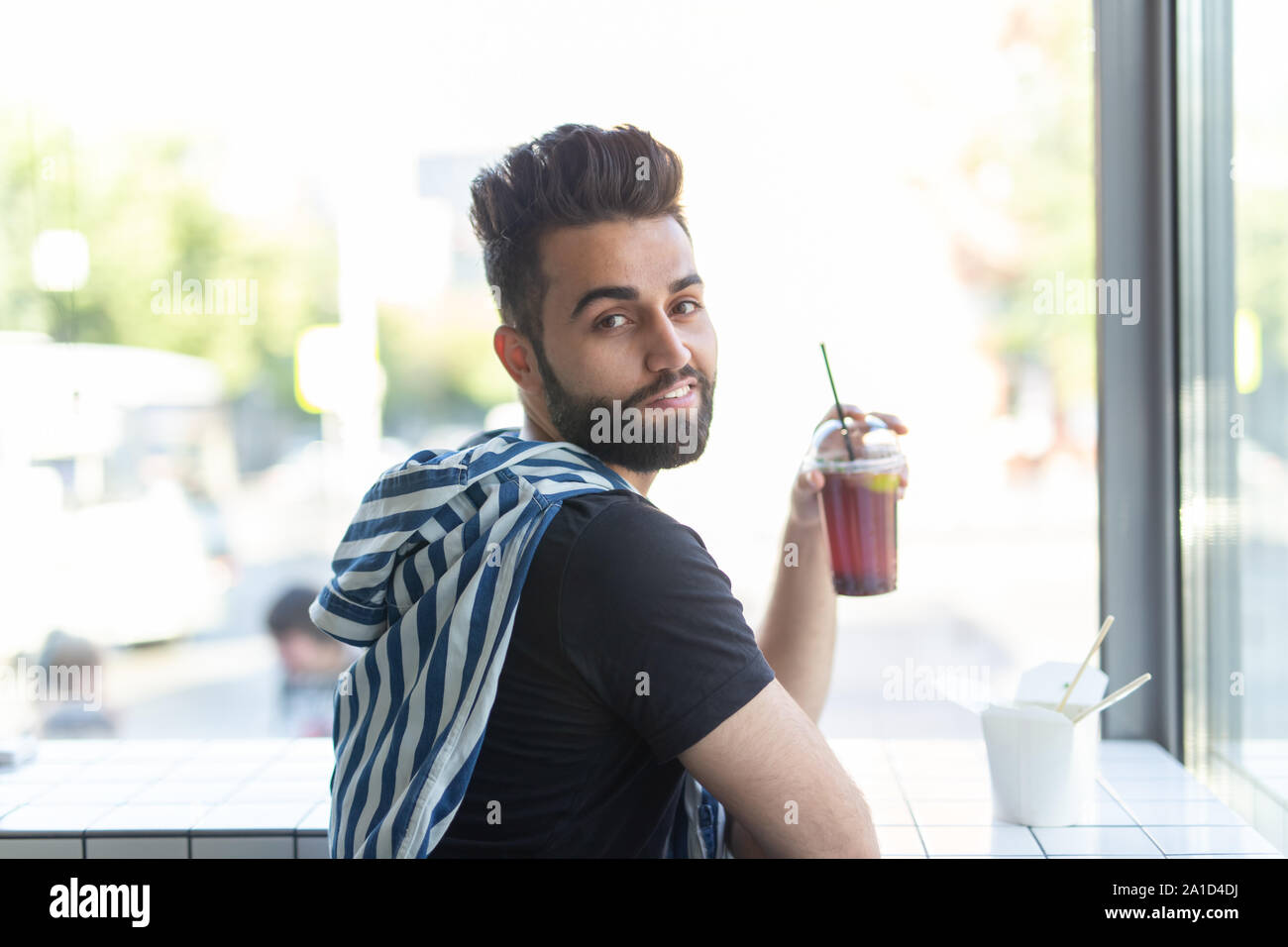 Positive young stylish guy drinking juice in a cafe during a break at ...
