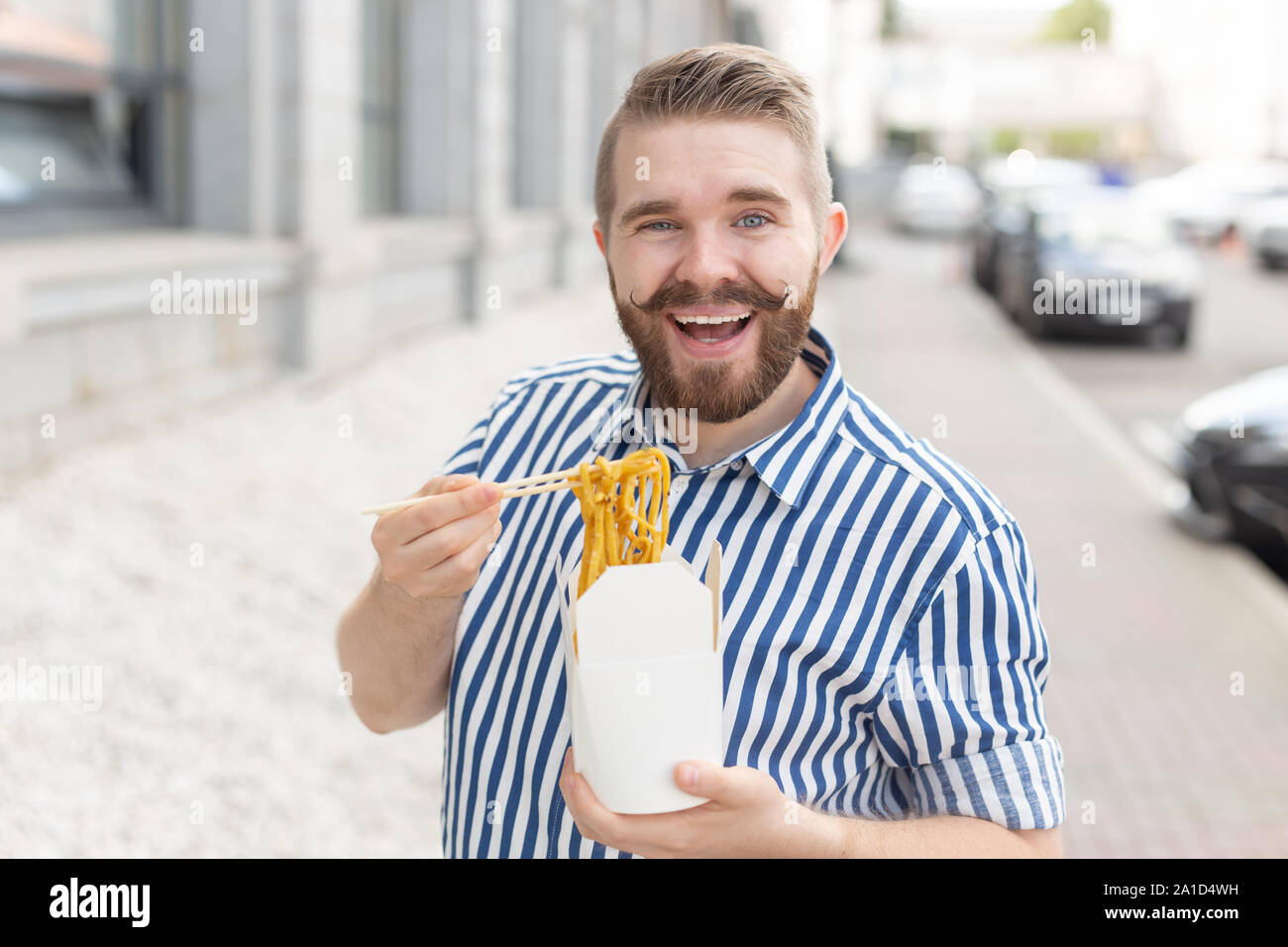 Young male hipster with a mustache and beard is eating chinese noodles ...