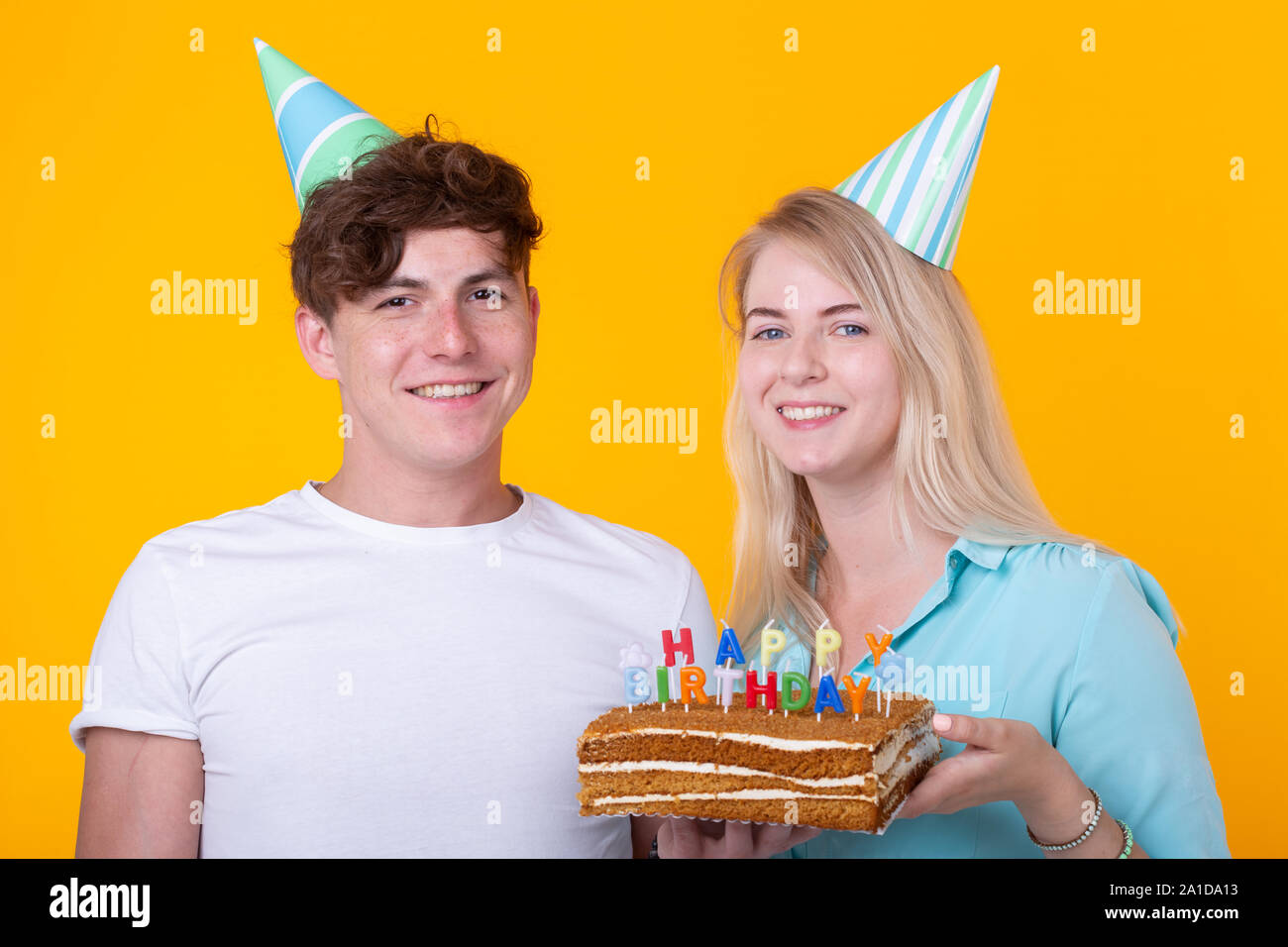 Funny young couple in paper caps and with a cake make a foolish face ...