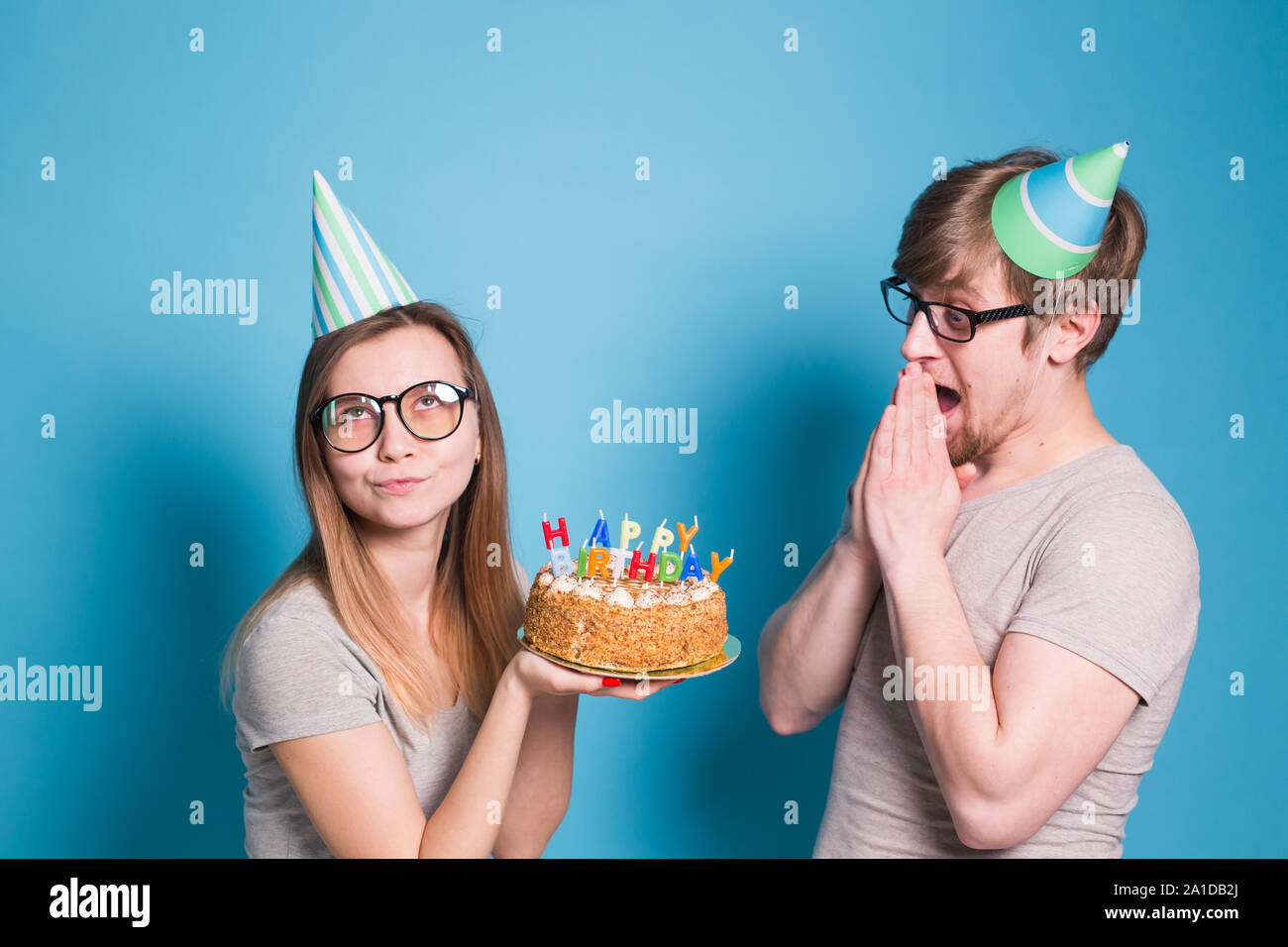 Funny young couple in paper caps and with a cake make a foolish face ...