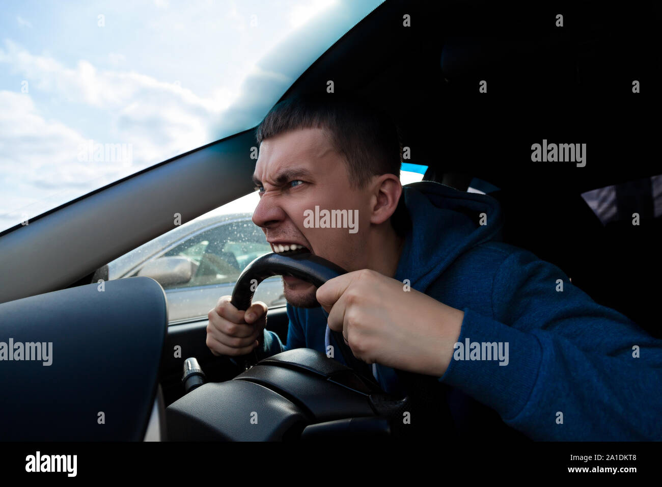 An emotional guy bites the steering wheel of a car while driving in a ...