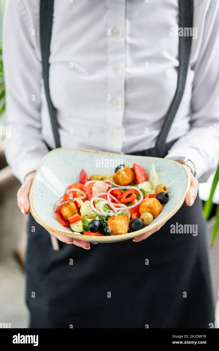 The waiter is holding a plate Traditional greek salad with fresh ...