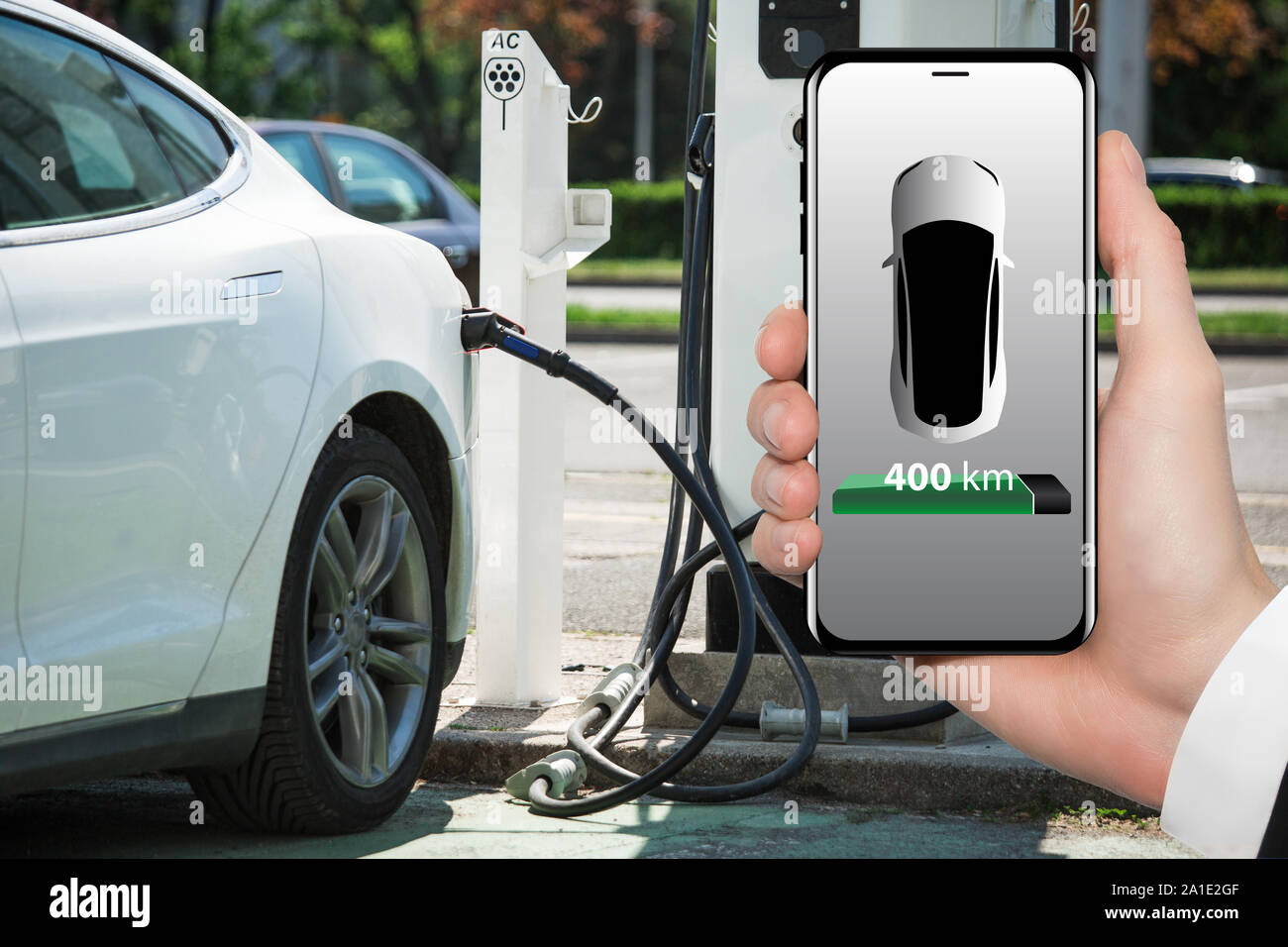 Hand with phone on a background of electric car charging point. On a ...