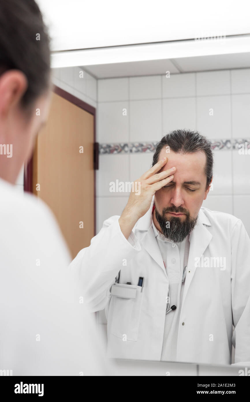 doctor in front of a mirror have headache and looks stressed near to an ...