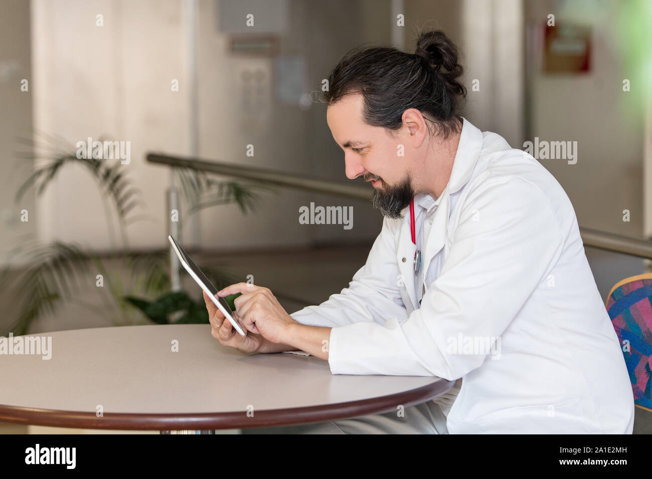 male doctor sitting behind a table and is using his tablet, doctor is ...