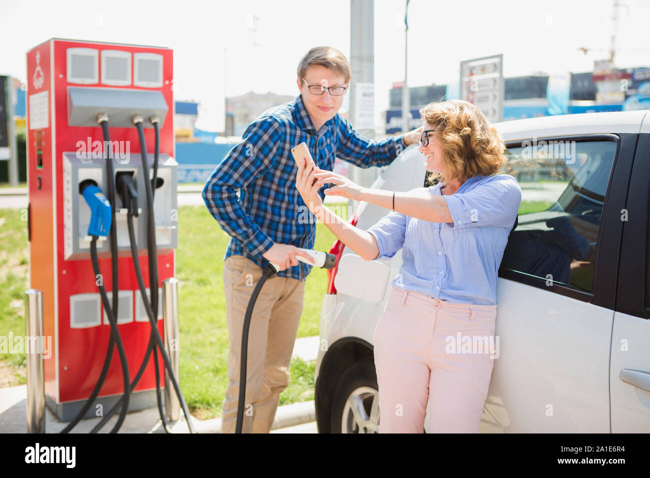 Man and woman are standing near the electric car. The car is charging ...