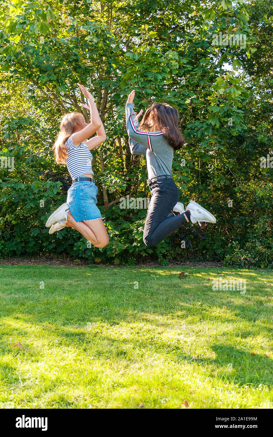Two teenagers girls jumping in a park in summertime. Having fun in ...