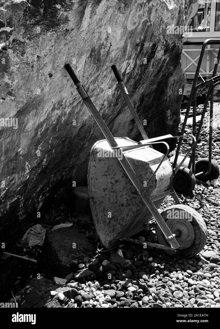 A wheelbarrow and trolley rest against a large rock in this black and ...