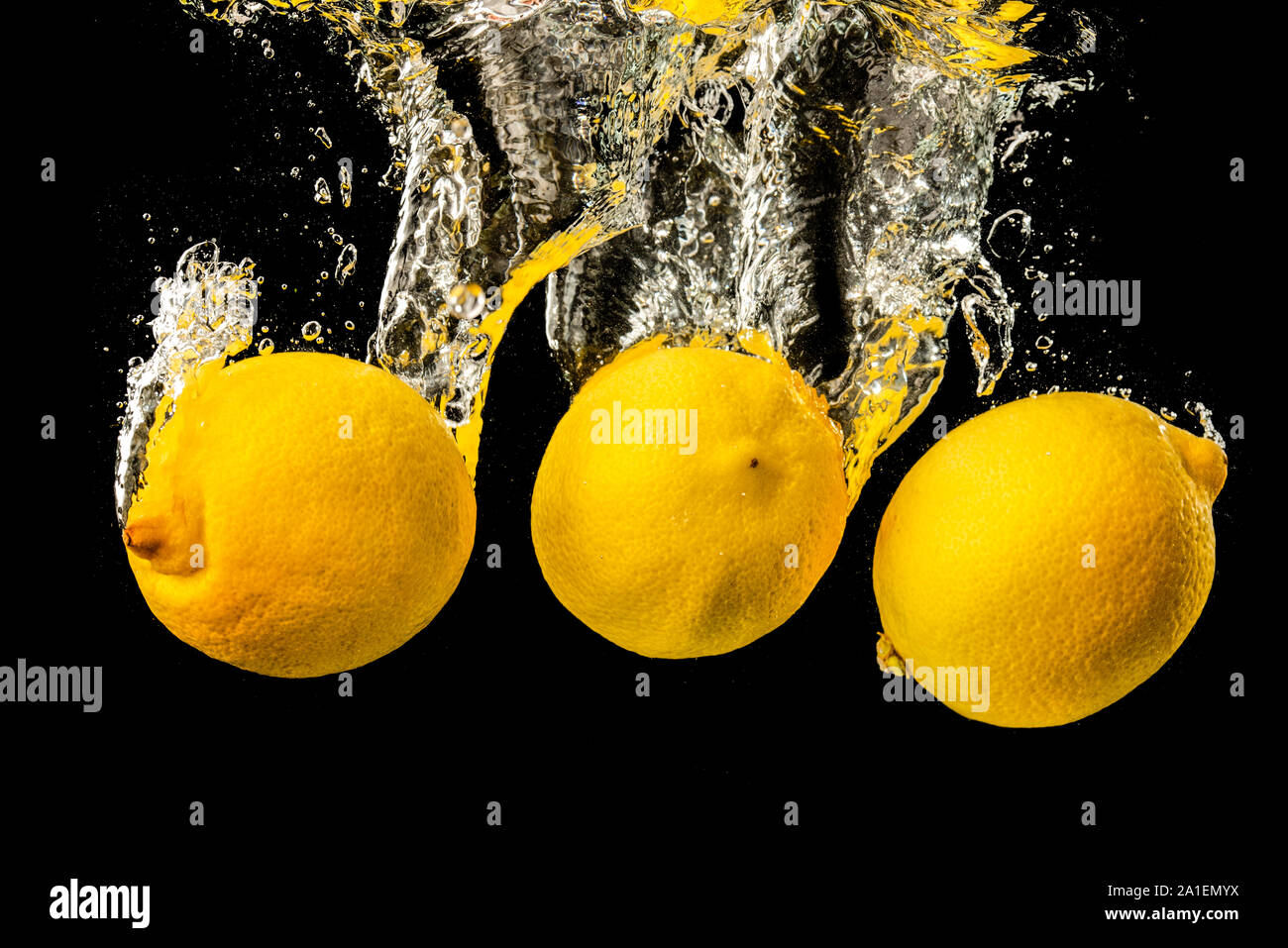 Fresh yellow lemons in water splash on black background with lots of ...