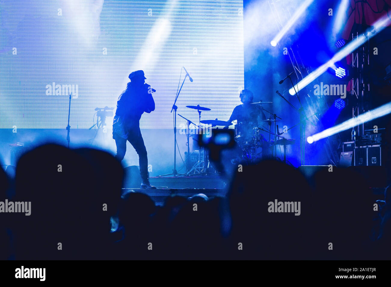 Silhouette of a big crowd at concert against a brightly lit stage ...