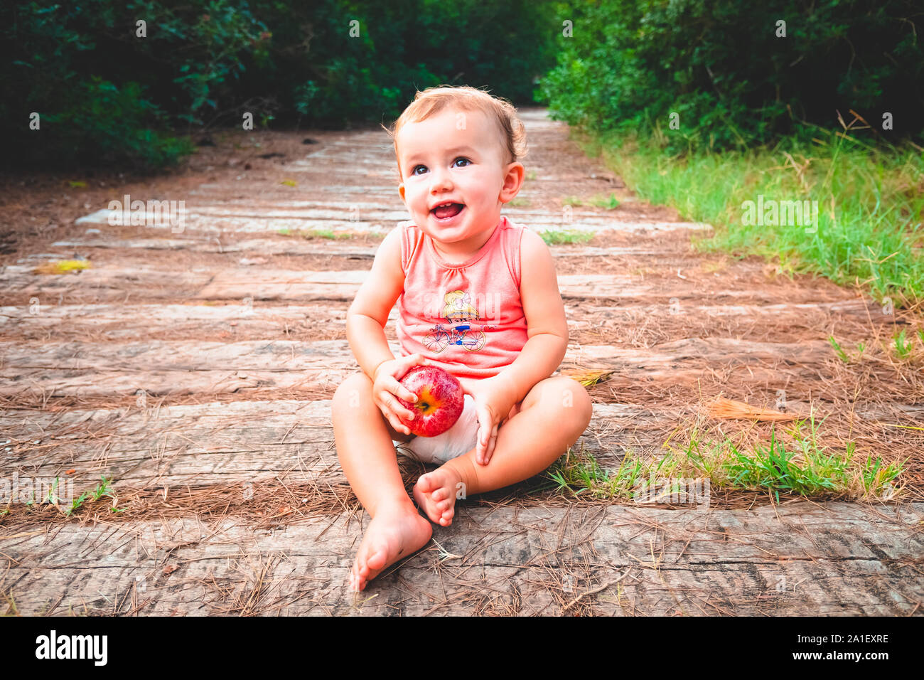 One year old baby sitting on a natural path laughing while holding an ...