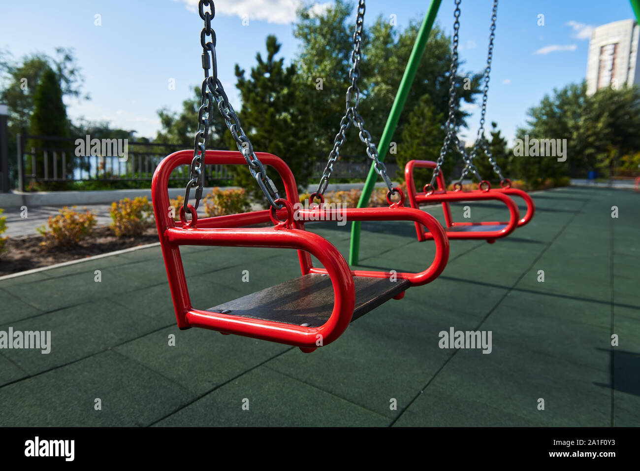 Empty red swings on the playground against blue sky and trees.. Swing ...