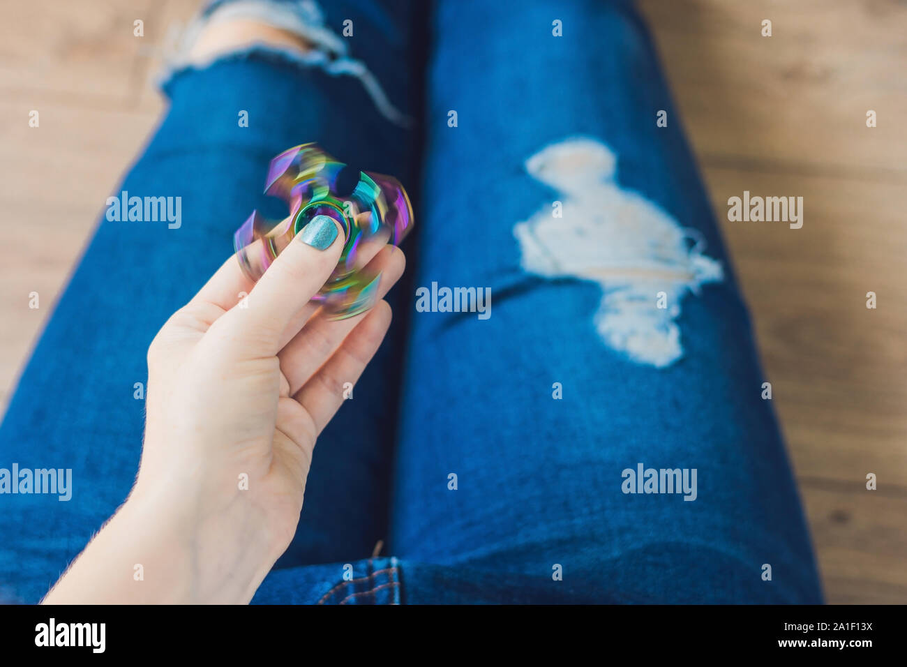 Girl teenager in holey jeans holds in hands and plays with spinner ...