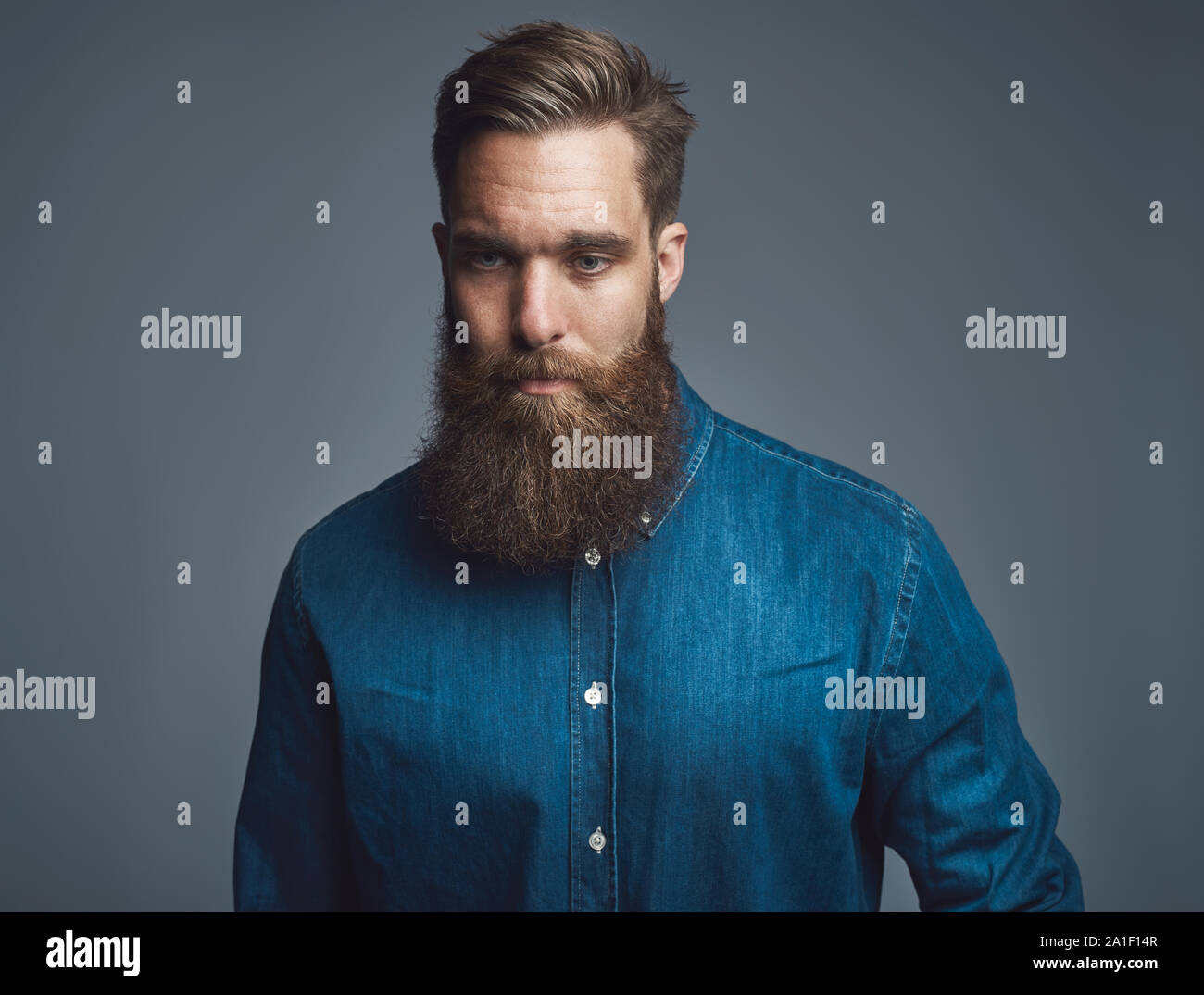 Hip and stylish young man with a long beard looking deep in thought ...