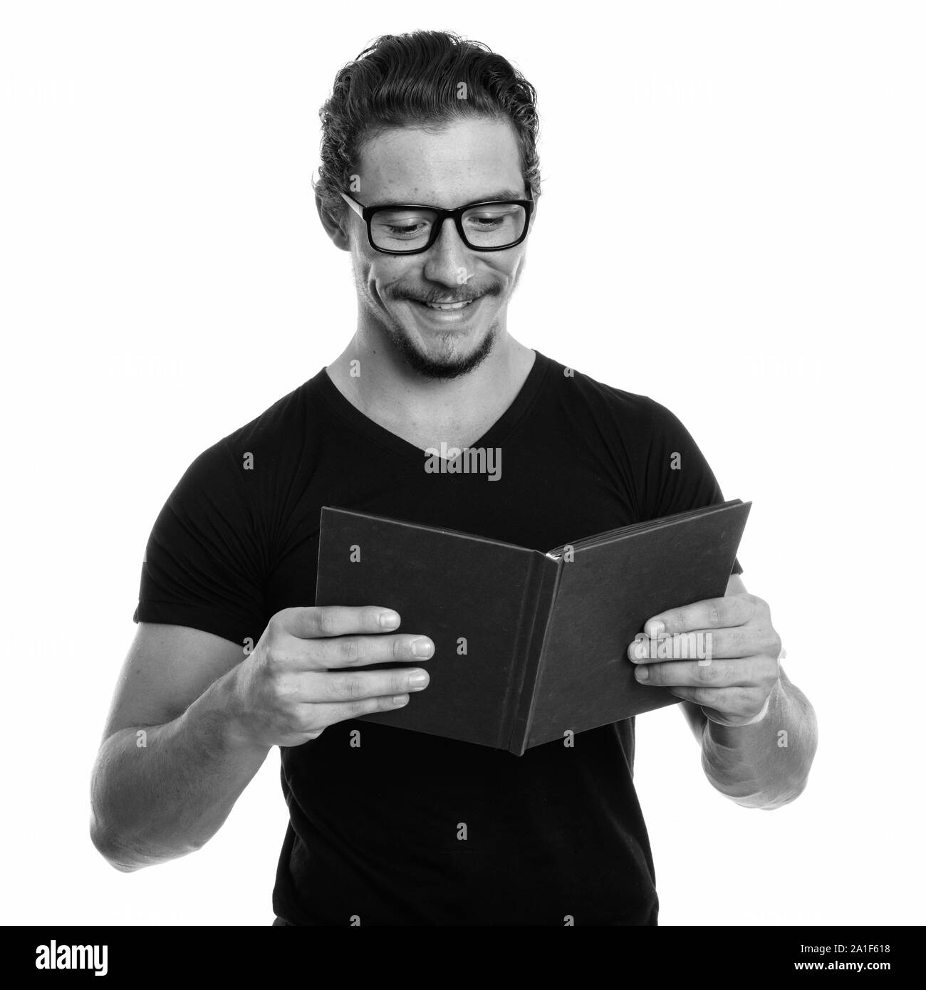 Studio shot of young happy man smiling while reading book with ...