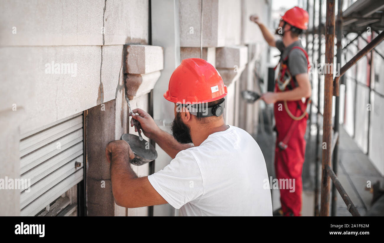 Two workers stands high on the scaffolding, plastering and renovating ...