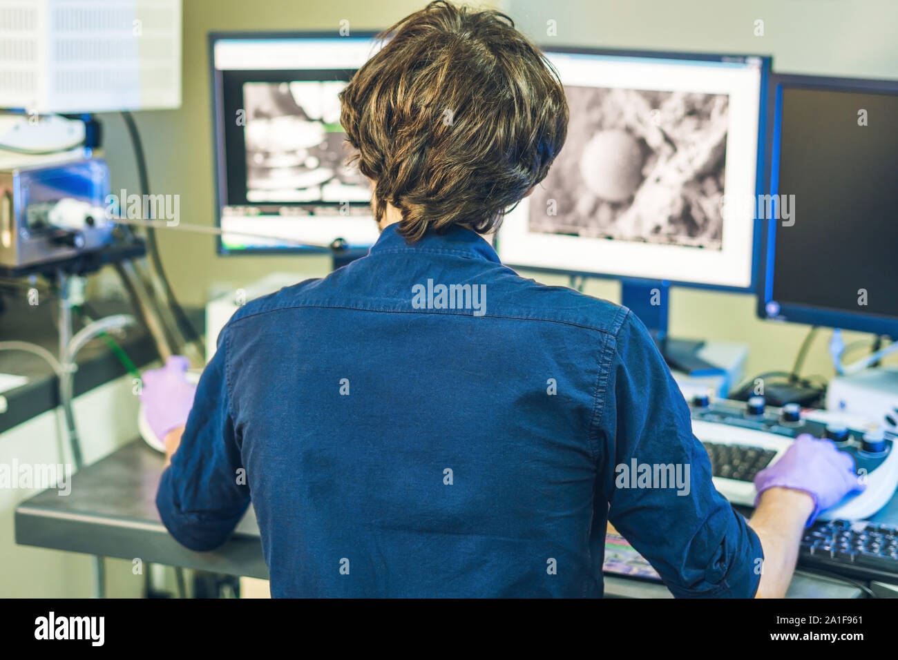 Scientist works at a electron microscope control pannel with two ...