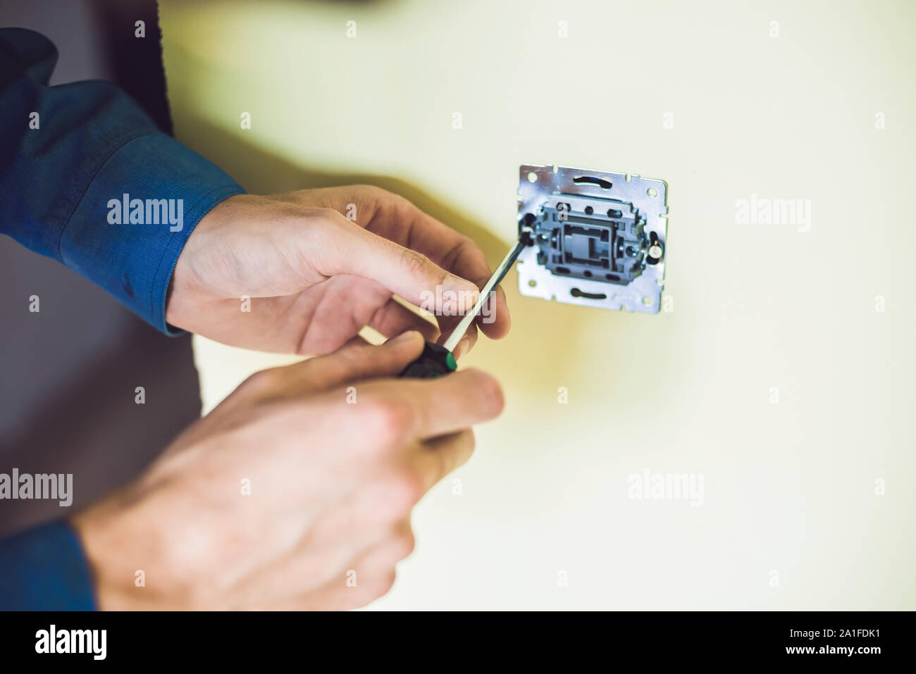 A young electrician installing an electrical switch in a new house ...