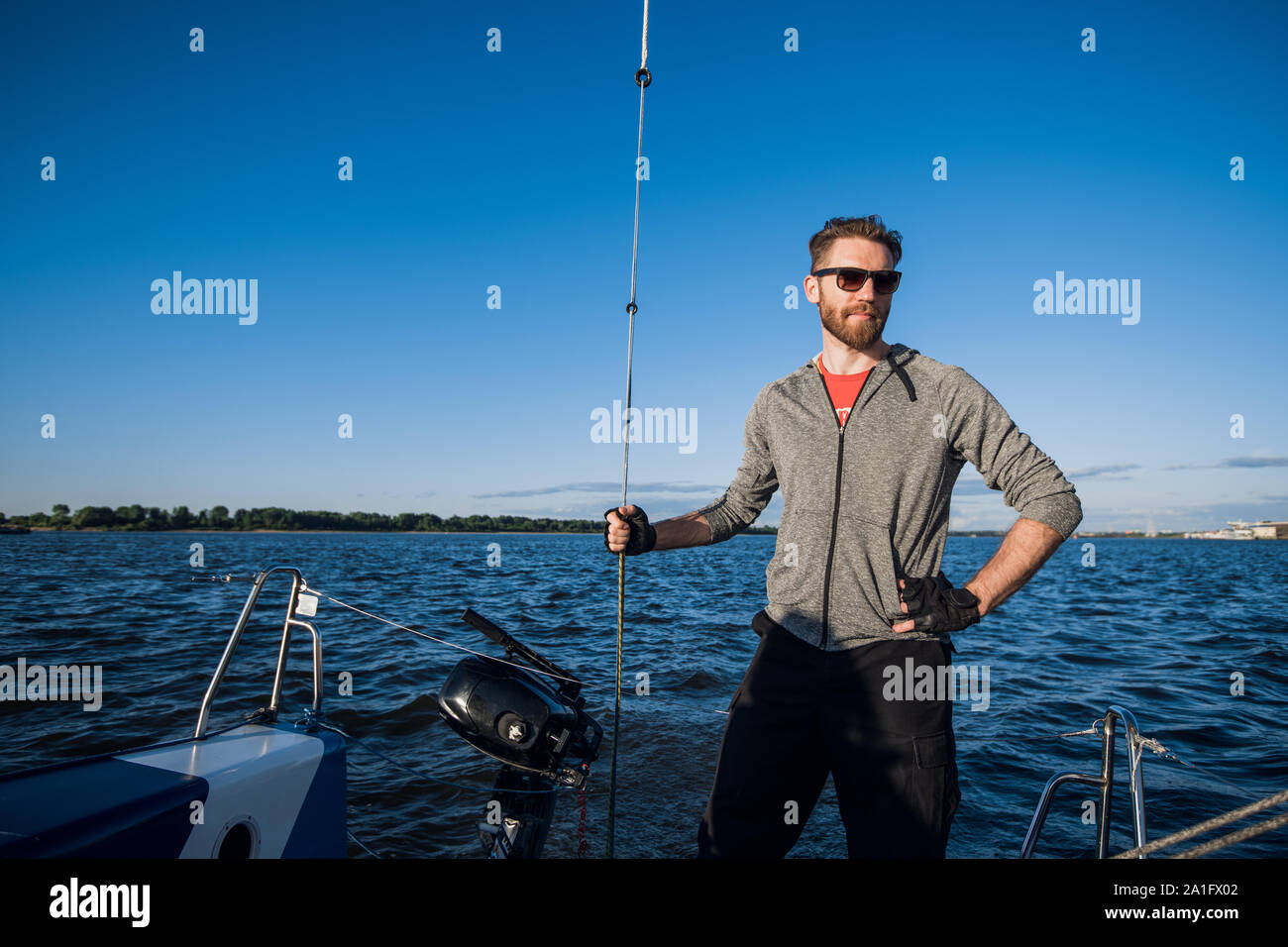Yacht captain with a beard stands on sail boom on a sailing yacht and ...