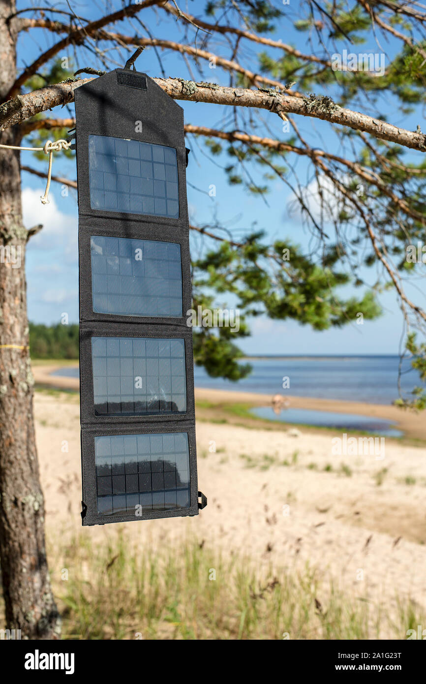 Portable foldable solar panel battery hanging on the outdoors on a pine ...