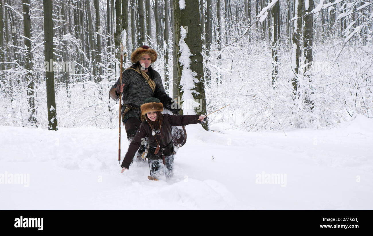 Father viking with his son going in the winter forest, they having axe ...