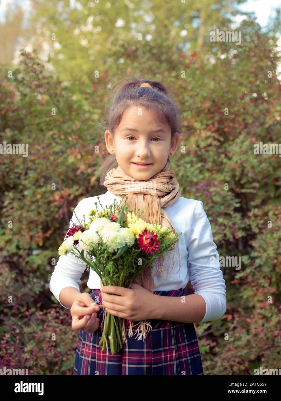 Serious little girl holding flowers and leaves bouquet. Child in school ...