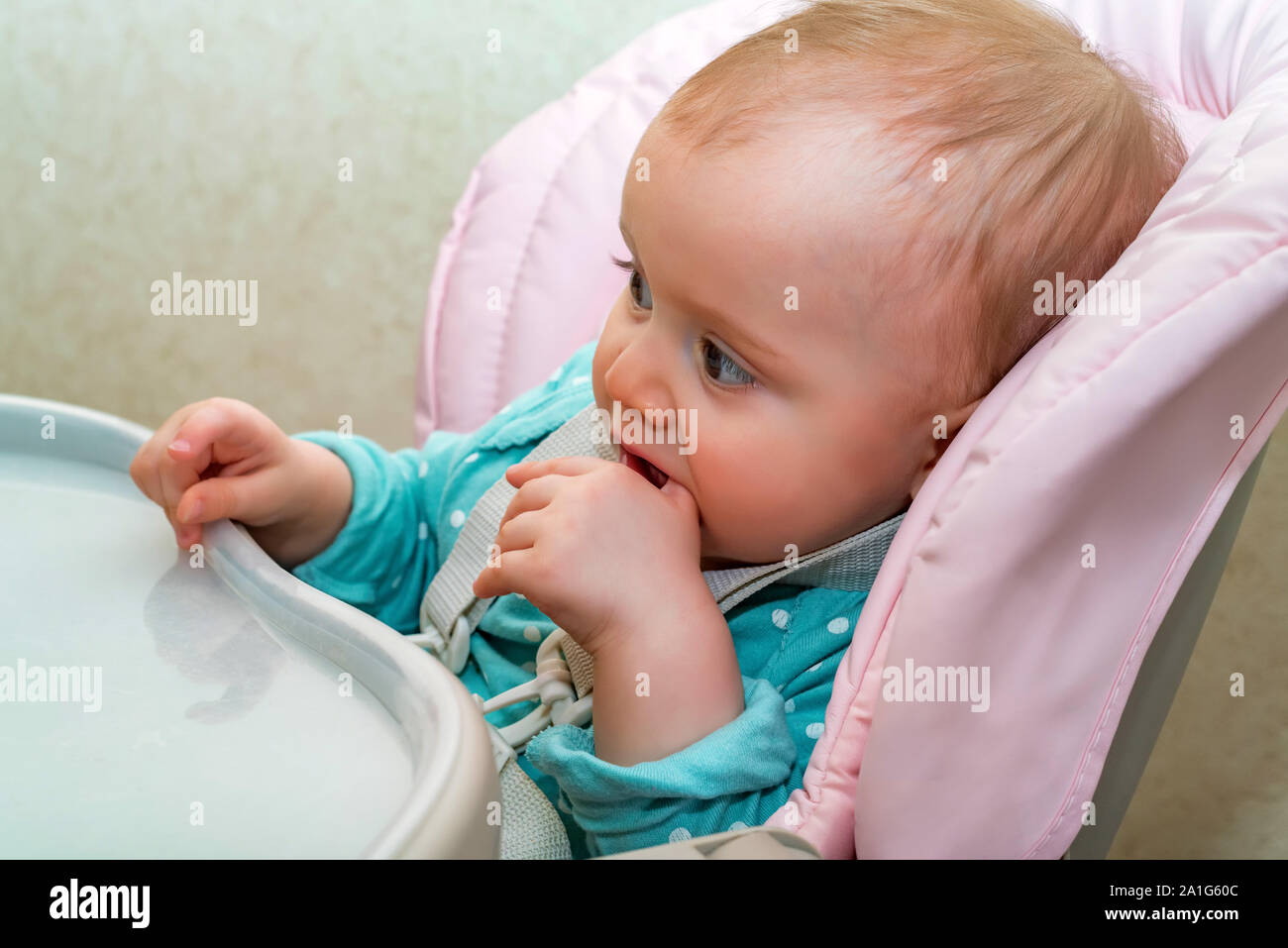 Close view of serious face of baby girl in pram putting her inger in ...