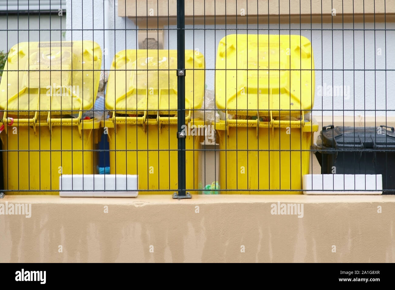 Yellow garbage cans stand in a row behind a mesh fence Stock Photo - Alamy