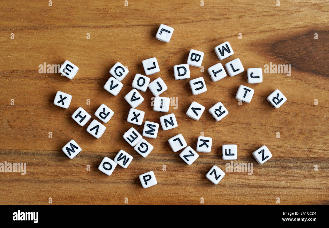 Small white cube beads with various letters scattered on wooden board ...