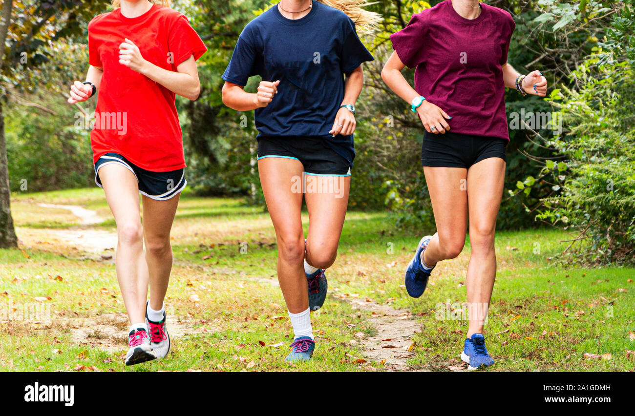 Three high school teenage girls are running together during cros ...