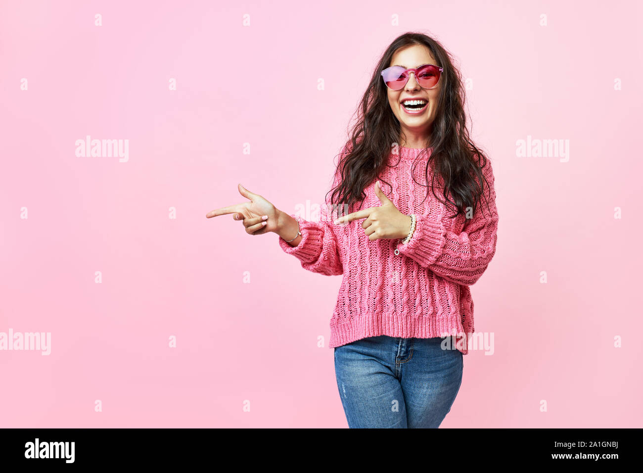 Positive attractive young female, points aside with cheerful expression ...