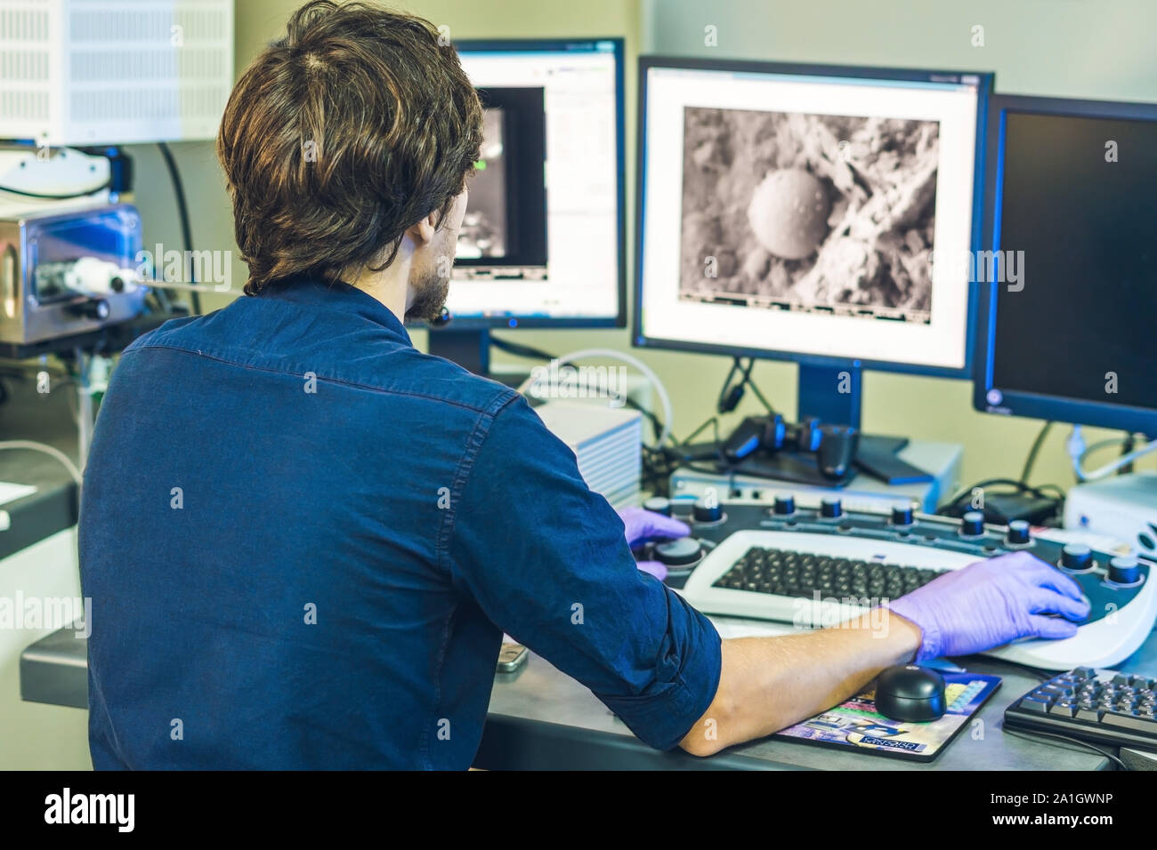 Scientist works at a electron microscope control pannel with two ...