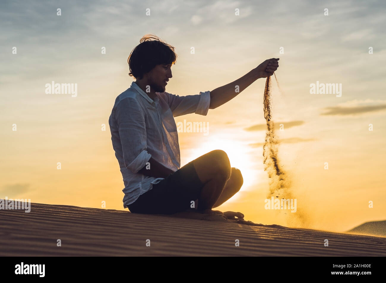 A man is pouring sand in the desert. Sand through the fingers of the ...