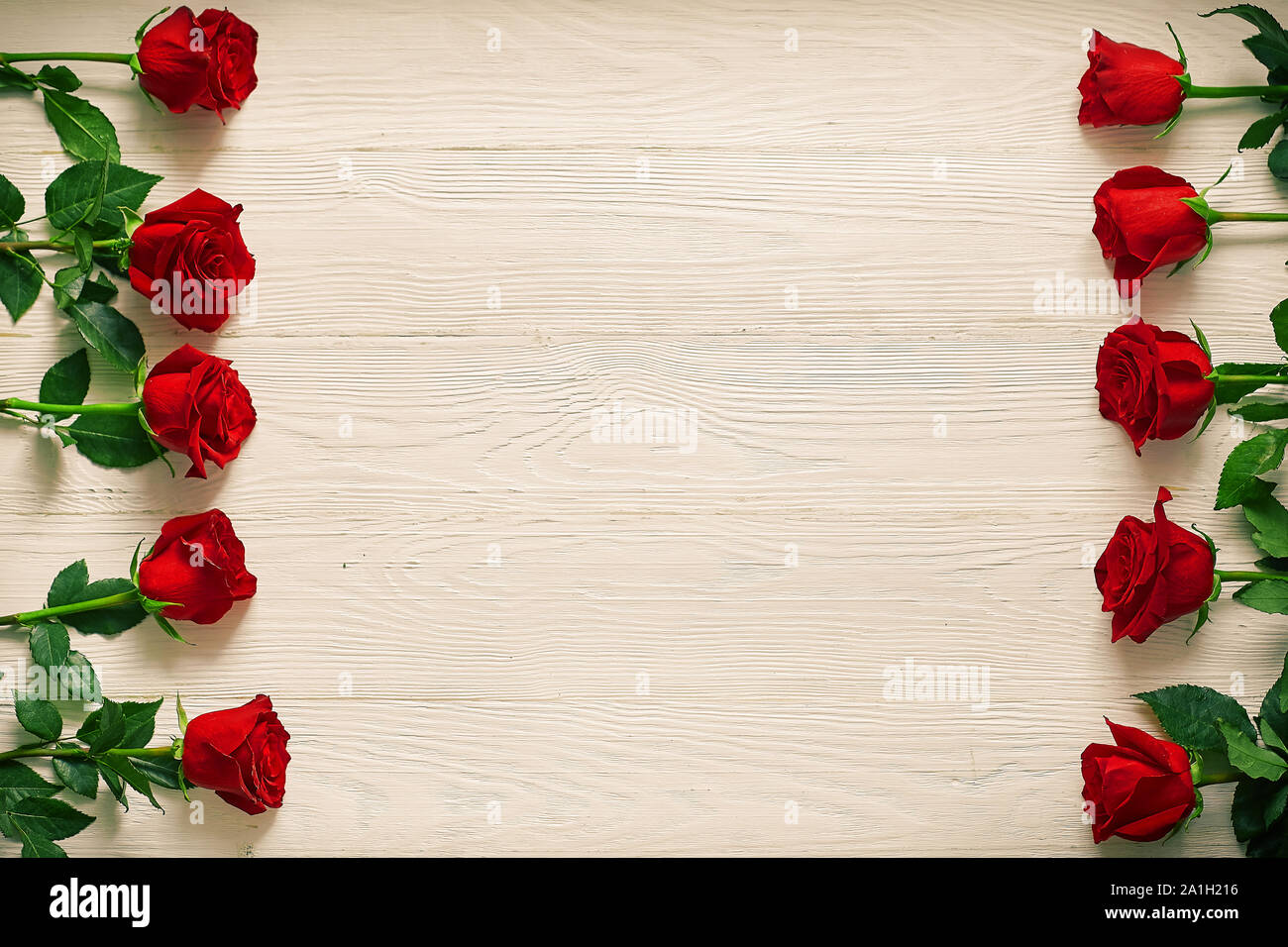 Frame of red roses on white wooden background. With space for text ...