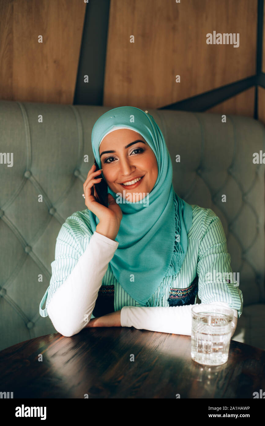 Beautiful young arabic girl in hijab talking by phone at cafe. Sunlight ...