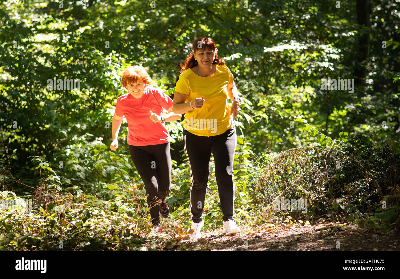 Two middle aged women running through a forest Stock Photo - Alamy