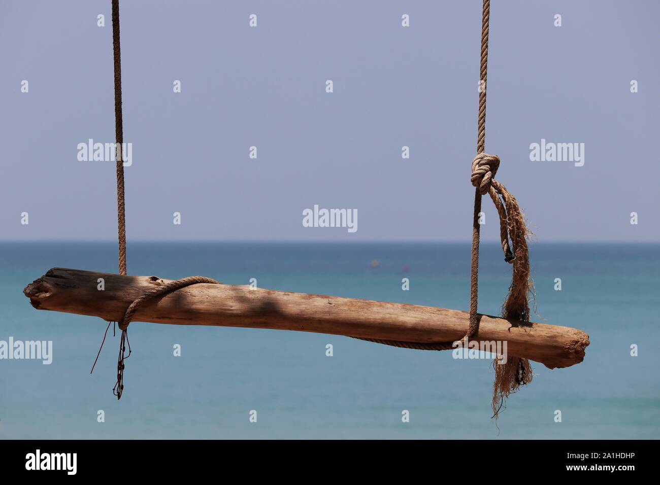 Swing of log and ropes on a background of blue sea and sky. Beach ...