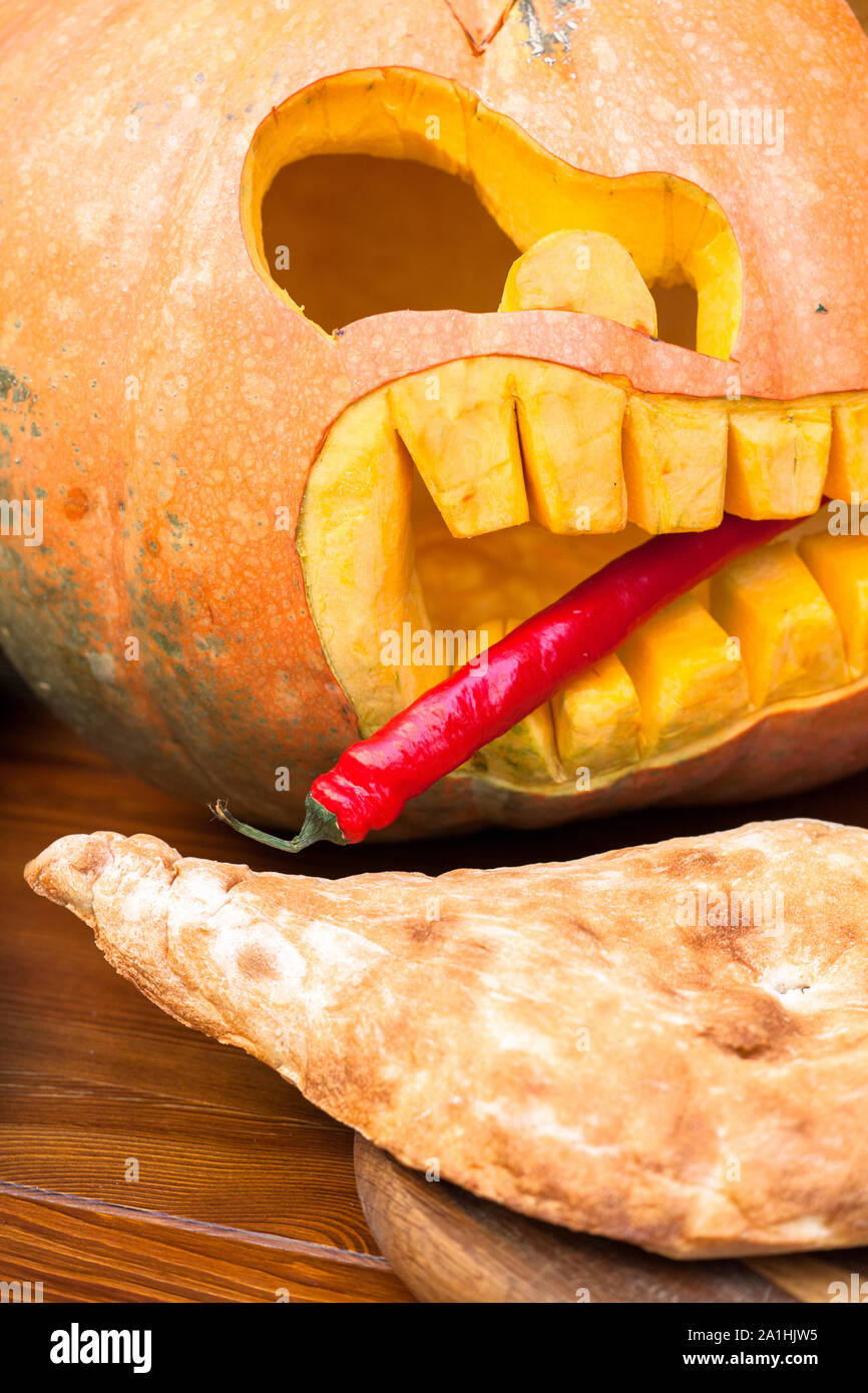 Hungry pumpkin with pepper. In mouth a pointy red pepper tongue sticks ...