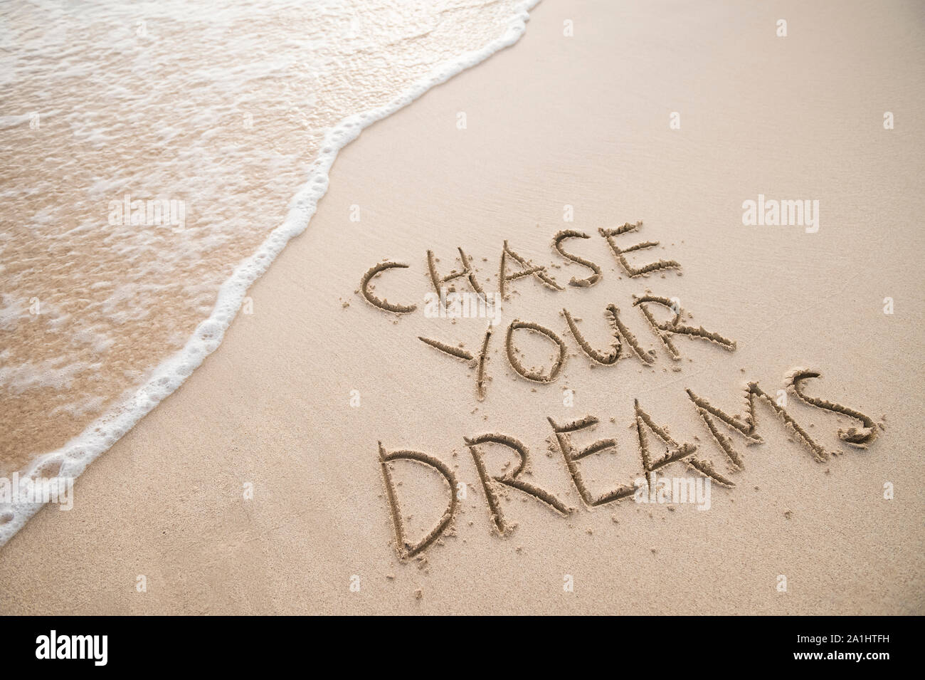 Chase Your Dreams travel message handwritten on smooth sand beach with ...