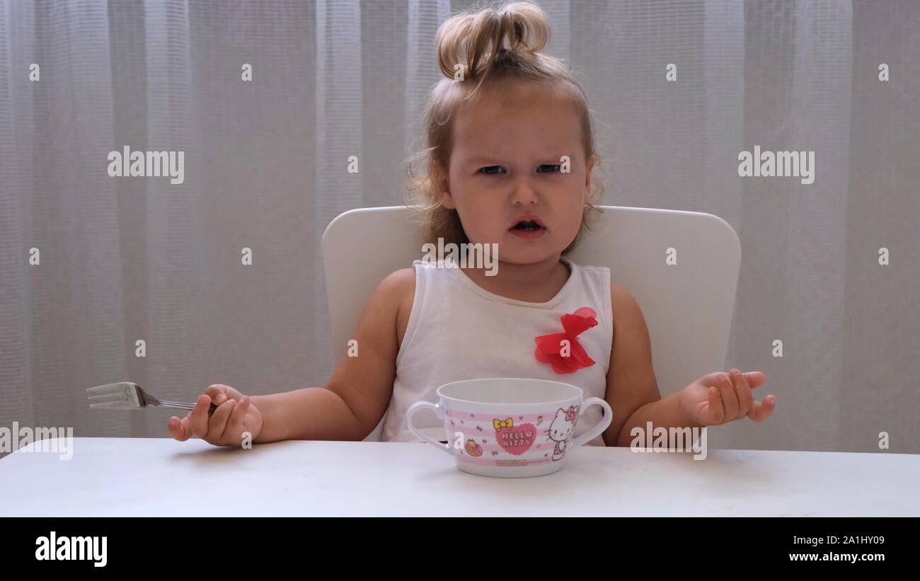 Infant girl eating baby food at a small childrens table on a white ...