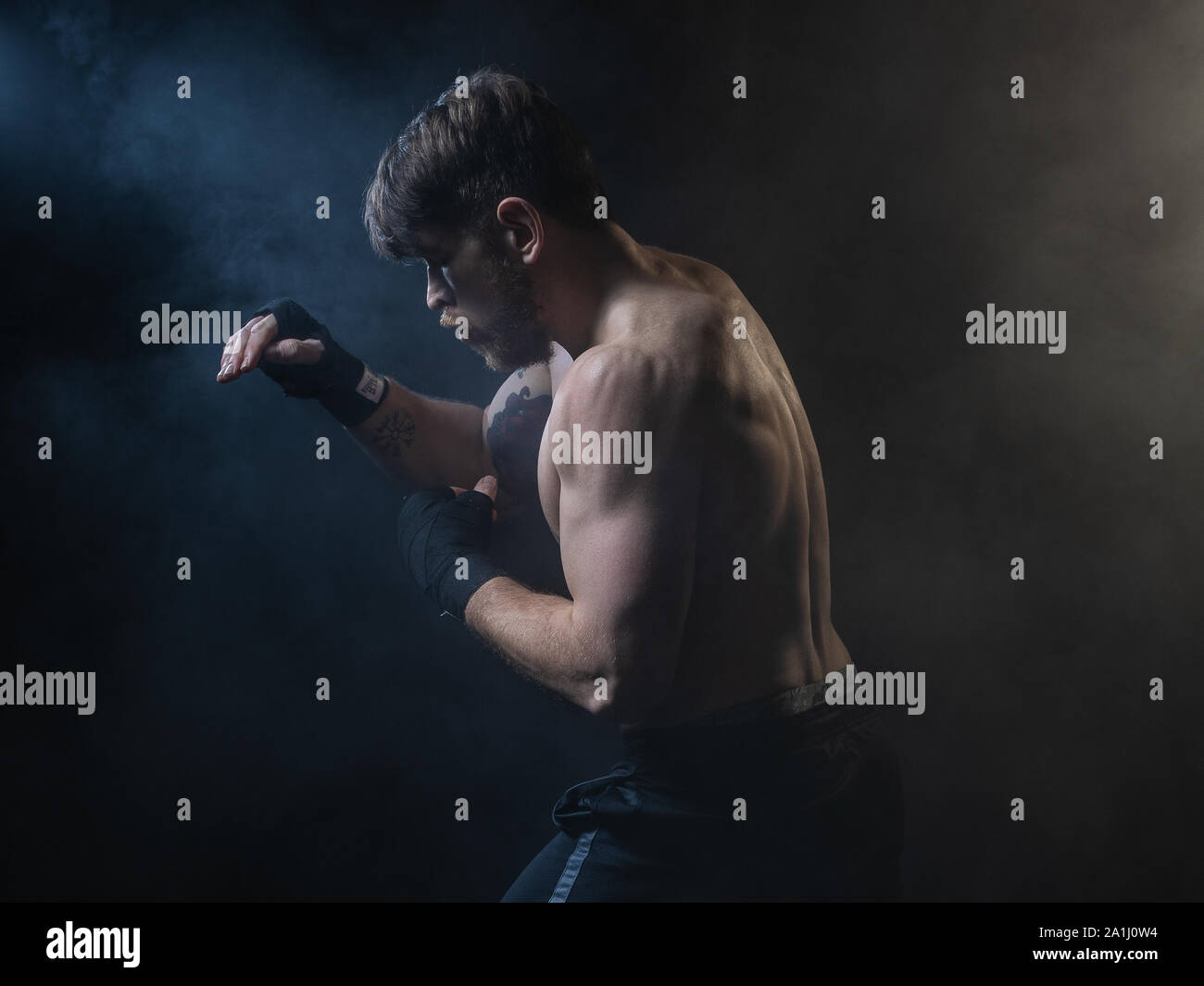 A young handsome bearded male shadow boxes in a dark and smoke filled ...